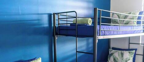Quarto com beliche, roupa de cama e almofadas azuis, uma toalha enrolada no beliche inferior e uma janela ao fundo.