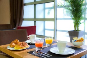 Uma mesa de café da manhã com croissants, suco de laranja e uma tigela de frutas.