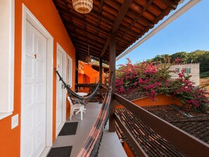 Varanda com rede, portas brancas e vista para flores cor-de-rosa e edifícios.
