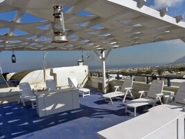 Terraço no telhado com cadeiras de lounge brancas e uma mesa, proporcionando vista da cidade e uma montanha ao longe.