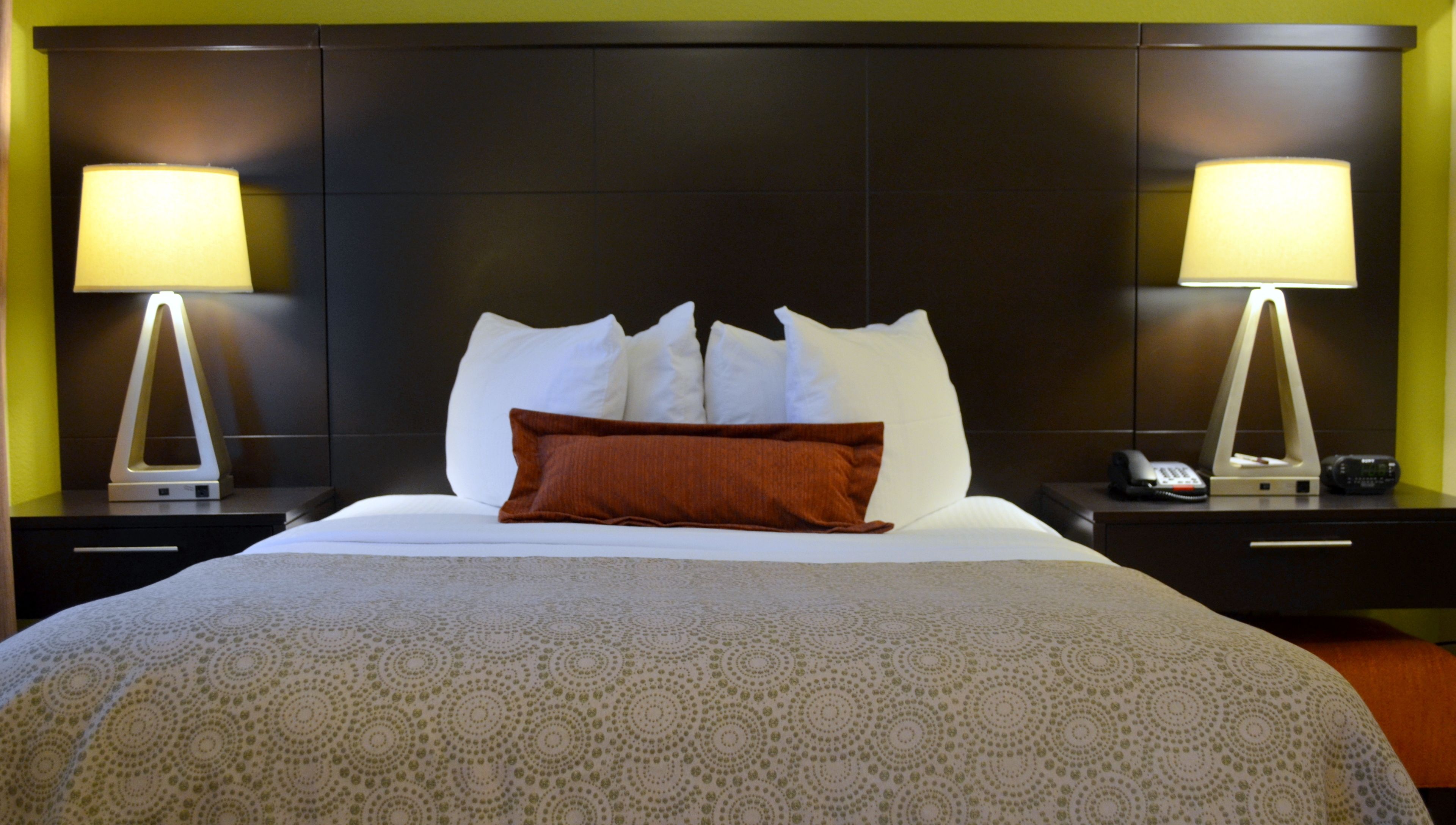 Quarto de hotel com uma cama grande, duas mesas de cabeceira e uma luminária em cada lado.