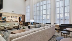 Um amplo hall de hotel com um sofá seccional grande, uma mesa de centro e uma área de refeições com uma mesa redonda e cadeiras.