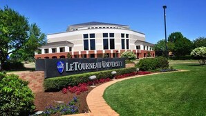 Edifício da LE TOURNEAU UNIVERSITY com placa, jardim ajardinado e céu azul límpido.