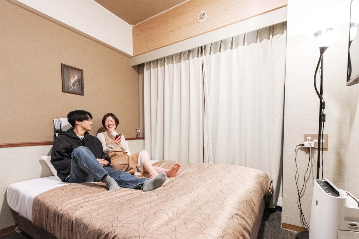 Quarto de hotel com uma cama, mesa de cabeceira, abajur e televisão.