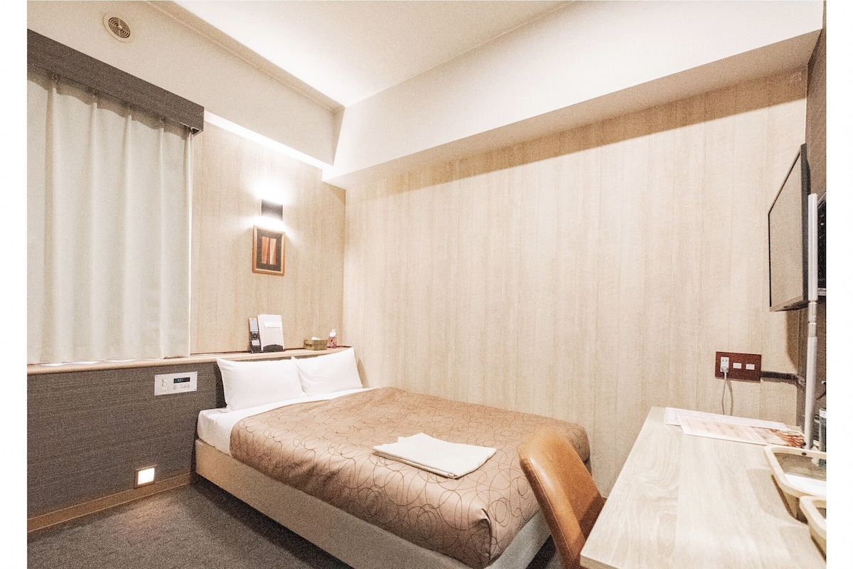 Quarto de hotel com cama, mesa de cabeceira, abajur e espelho.