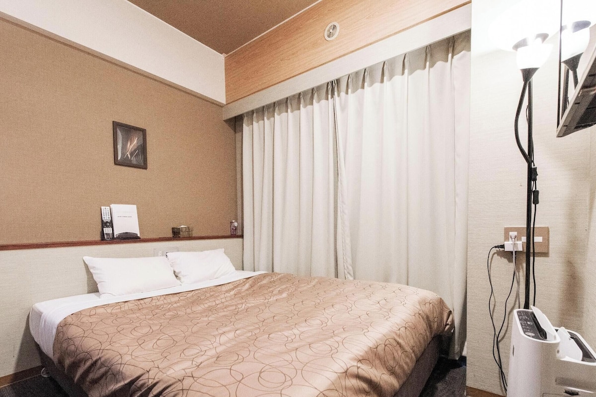Quarto de hotel com cama, escrivaninha, telefone e abajur.