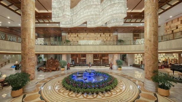 Um hall de hotel com vários níveis, uma fonte central, tetos altos e colunas de mármore.