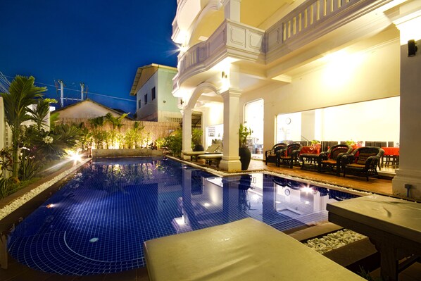Piscina interior com chão ladrilhado, rodeada por espreguiçadeiras e um bar com assentos.