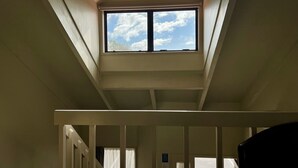 Um quarto com um claraboia, uma escada e uma porta que dá para outro cômodo.