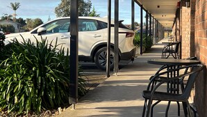 Área externa coberta com um SUV branco estacionado, mesas ao ar livre e uma parede de tijolos.
