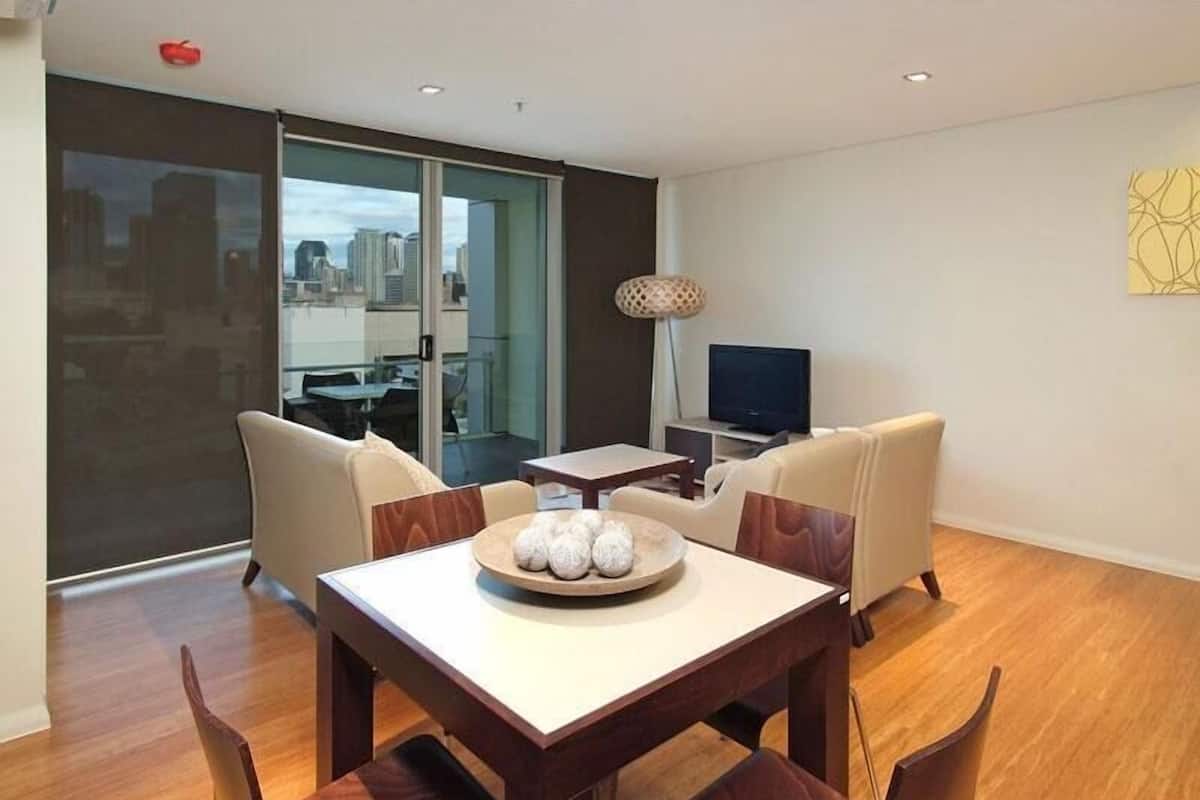 Uma sala de estar moderna com uma mesa de jantar, cadeiras, uma televisão e uma janela grande com vista para a cidade.