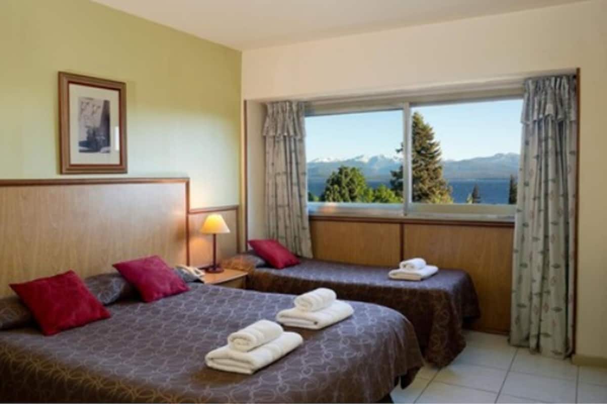 Quarto de hotel com duas camas, janela com vista para as montanhas e um quadro na parede.