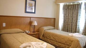 Quarto de hotel com duas camas, mesa de cabeceira com abajur e quadro na parede.