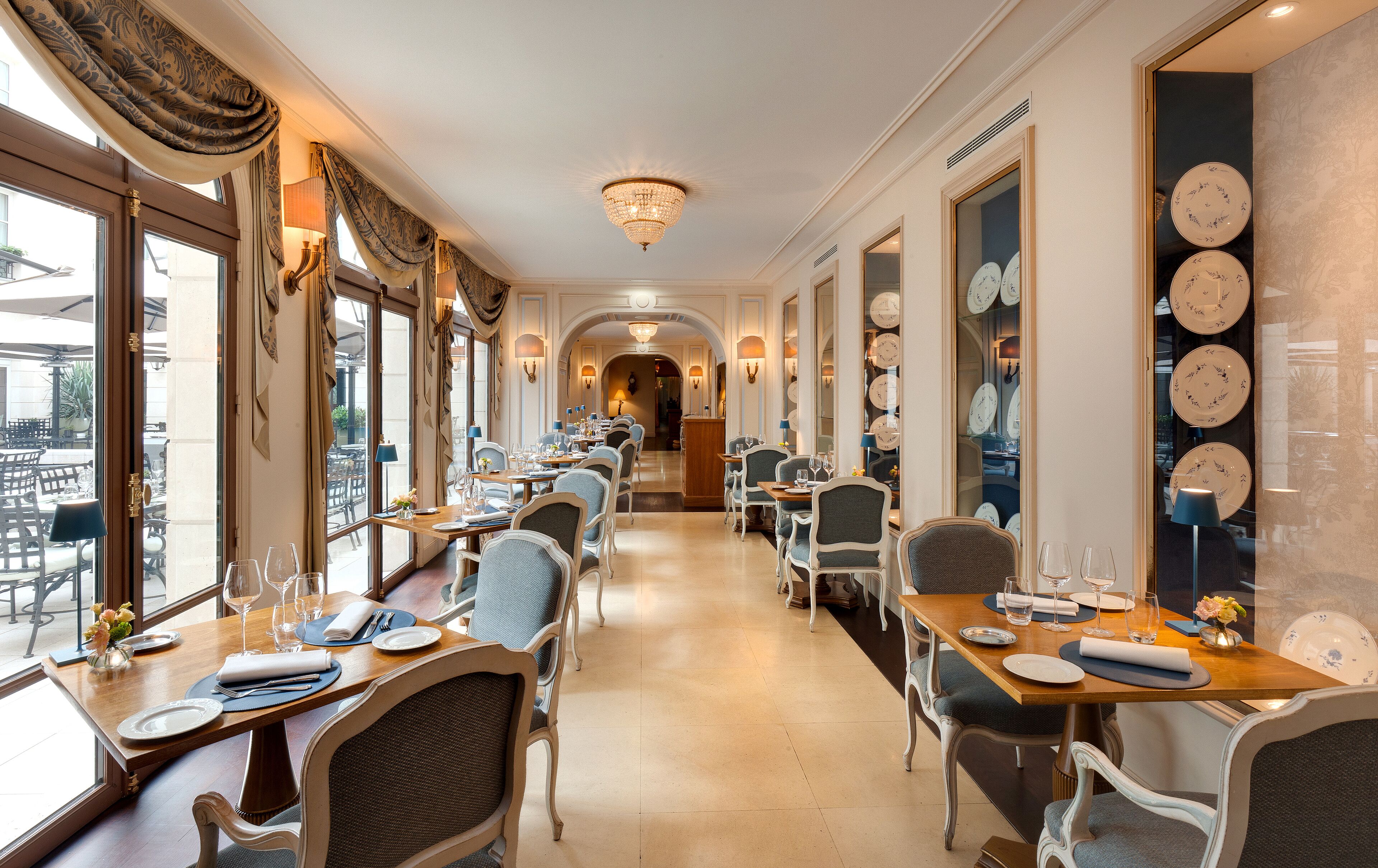 Um restaurante com um corredor comprido, mesas, cadeiras e um candelabro.