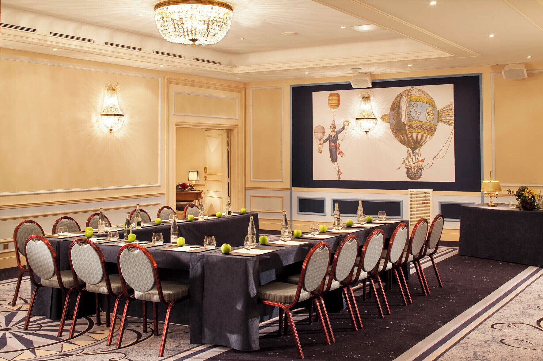 Sala de conferências com uma longa mesa, cadeiras e um candelabro.