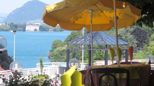 Um terraço com guarda-sóis amarelos, vista para um lago e um coreto.