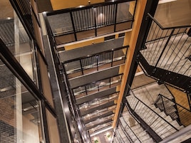 Interior com vários níveis, átrio central, guarda-corpos de vidro e design moderno.