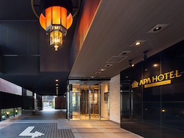 Exterior do APA HOTEL com entrada moderna, porta de vidro e placa exibindo o nome do hotel.