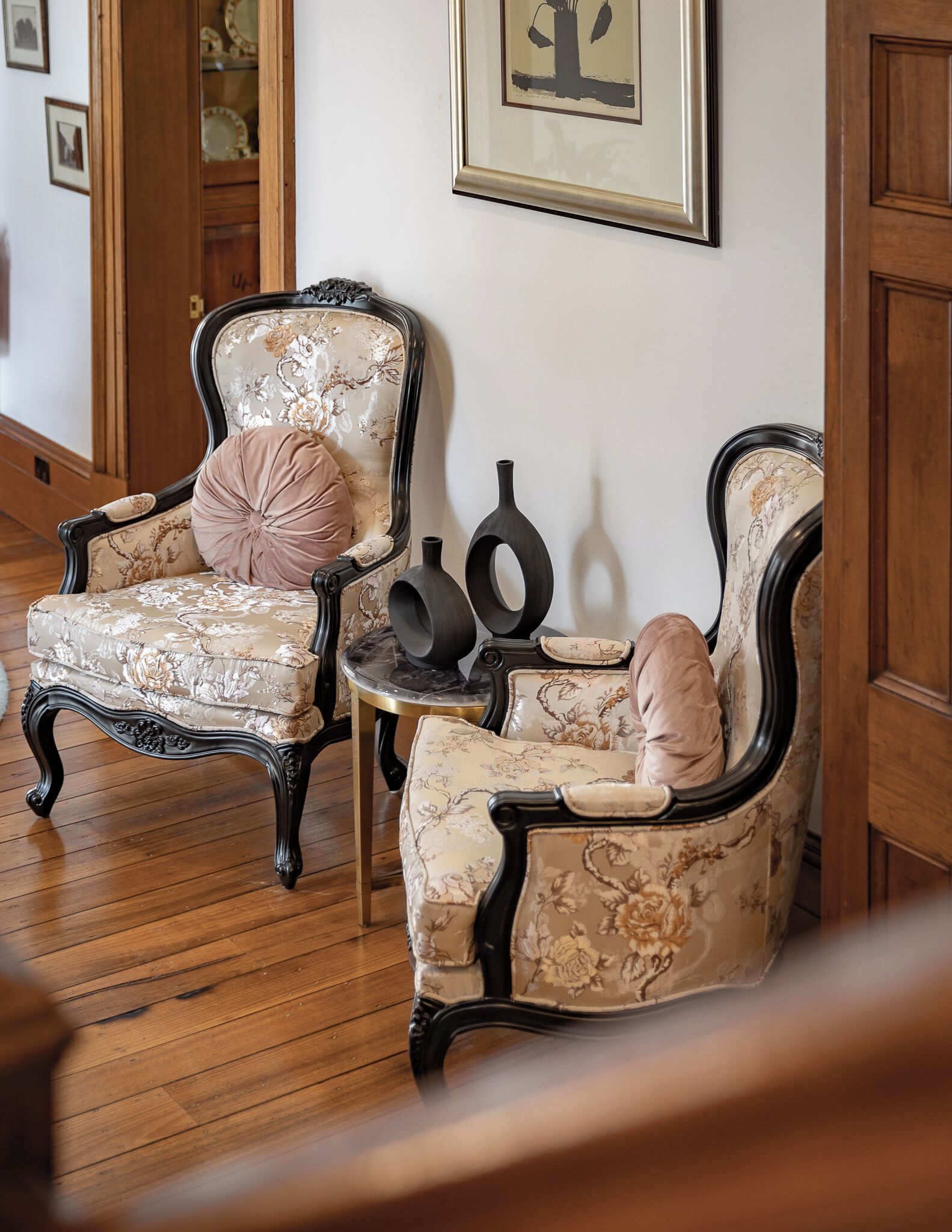 Duas poltronas ornamentadas com estofamento floral e detalhes em preto, sobre um piso de madeira polida.