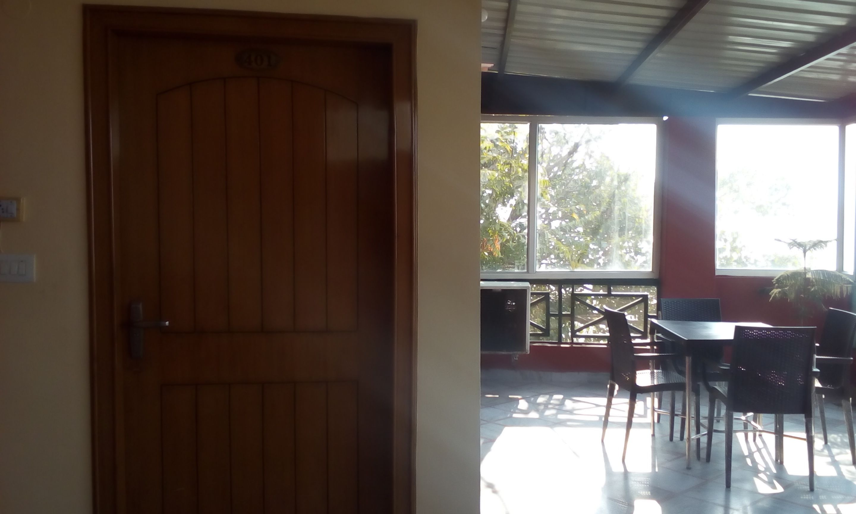 Quarto com porta de madeira, varanda com mesa e cadeiras, e janelas amplas.