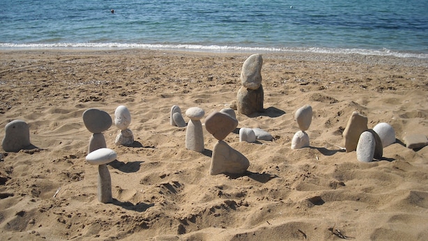 Uma praia arenosa com várias pedras grandes e lisas dispostas em círculo.