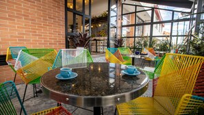 Uma mesa redonda com cadeiras e uma xícara de café, cercada por uma parede de tijolos e grandes janelas.