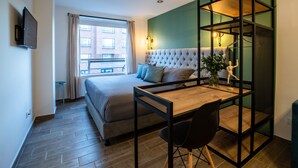 Quarto moderno com cama, escrivaninha e cadeira. Há uma janela com cortinas, TV na parede e uma parede verde de destaque.