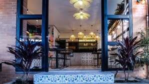Um restaurante com fachada de tijolos, grandes janelas e luminárias pendentes.