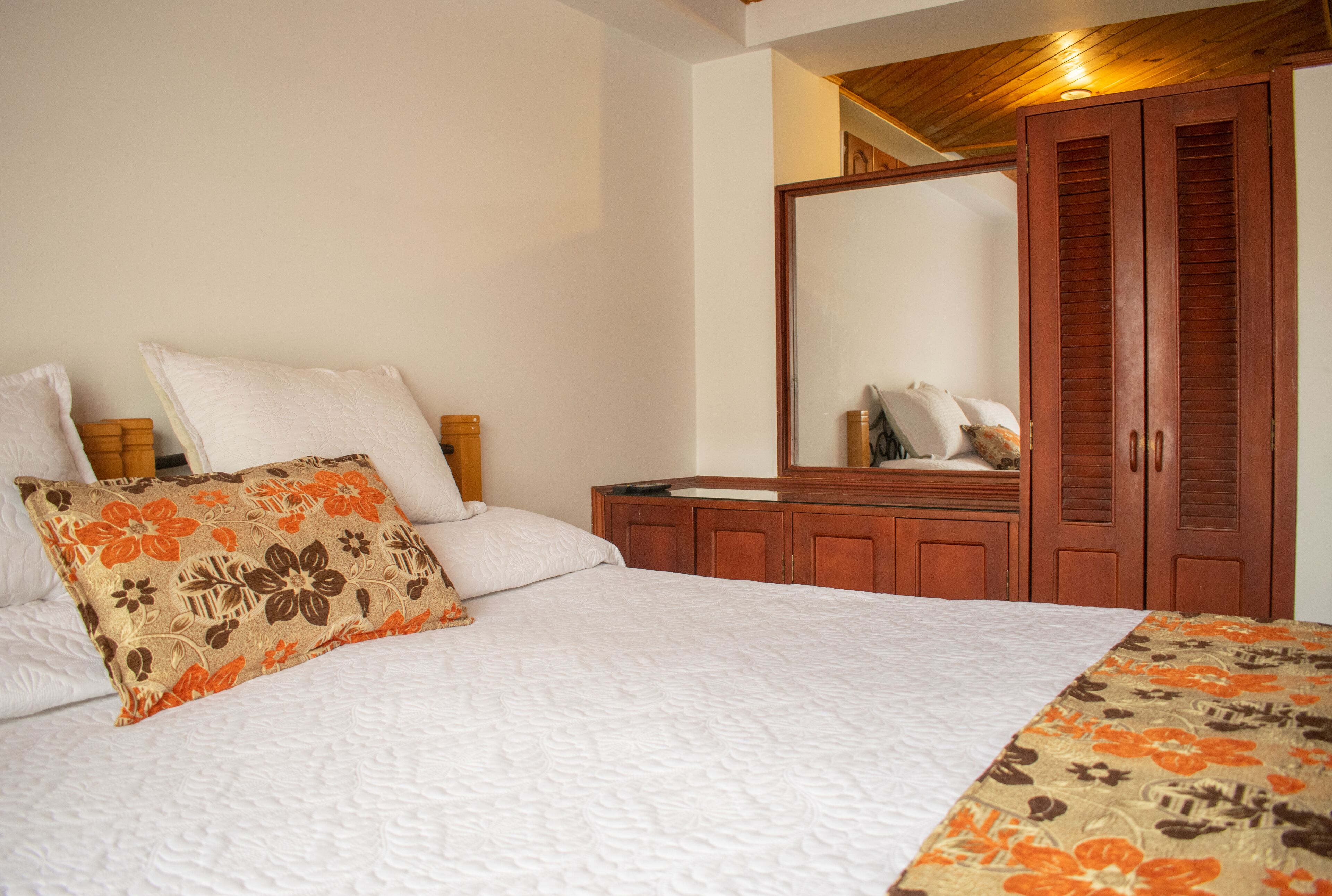 Um quarto com cama, guarda-roupa de madeira, mesa de cabeceira e espelho.
