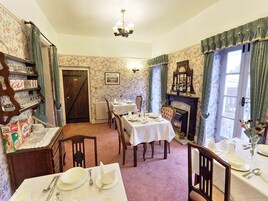 Uma sala de jantar com lareira, estante de livros e mesa posta para quatro pessoas.