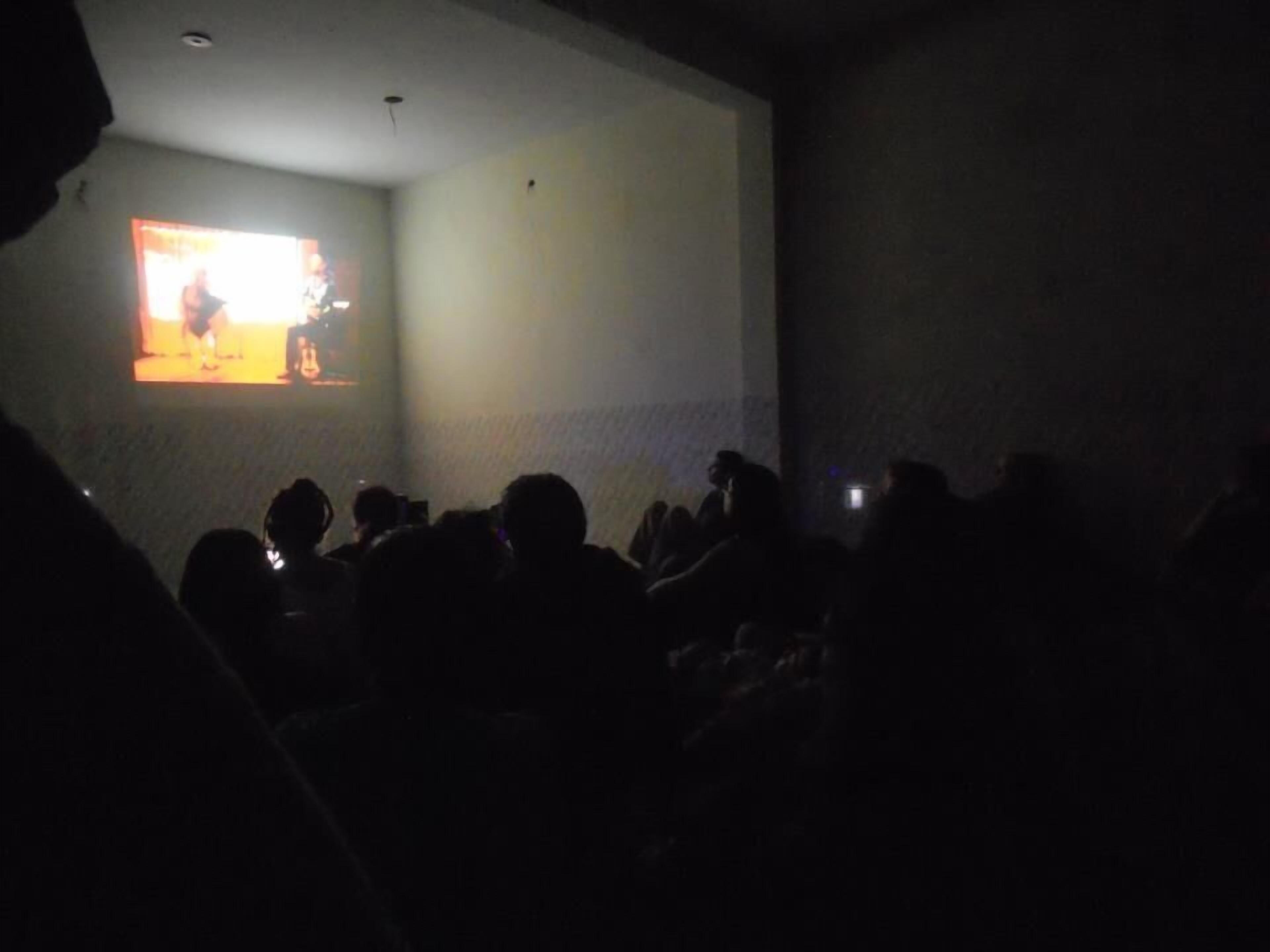 Um auditório com pouca luz, palco e plateia acomodada em fileiras.