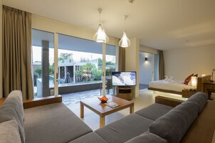 Sala de estar moderna com sofá, mesa de centro e televisão. Possui uma varanda com vista para edifícios e vegetação.