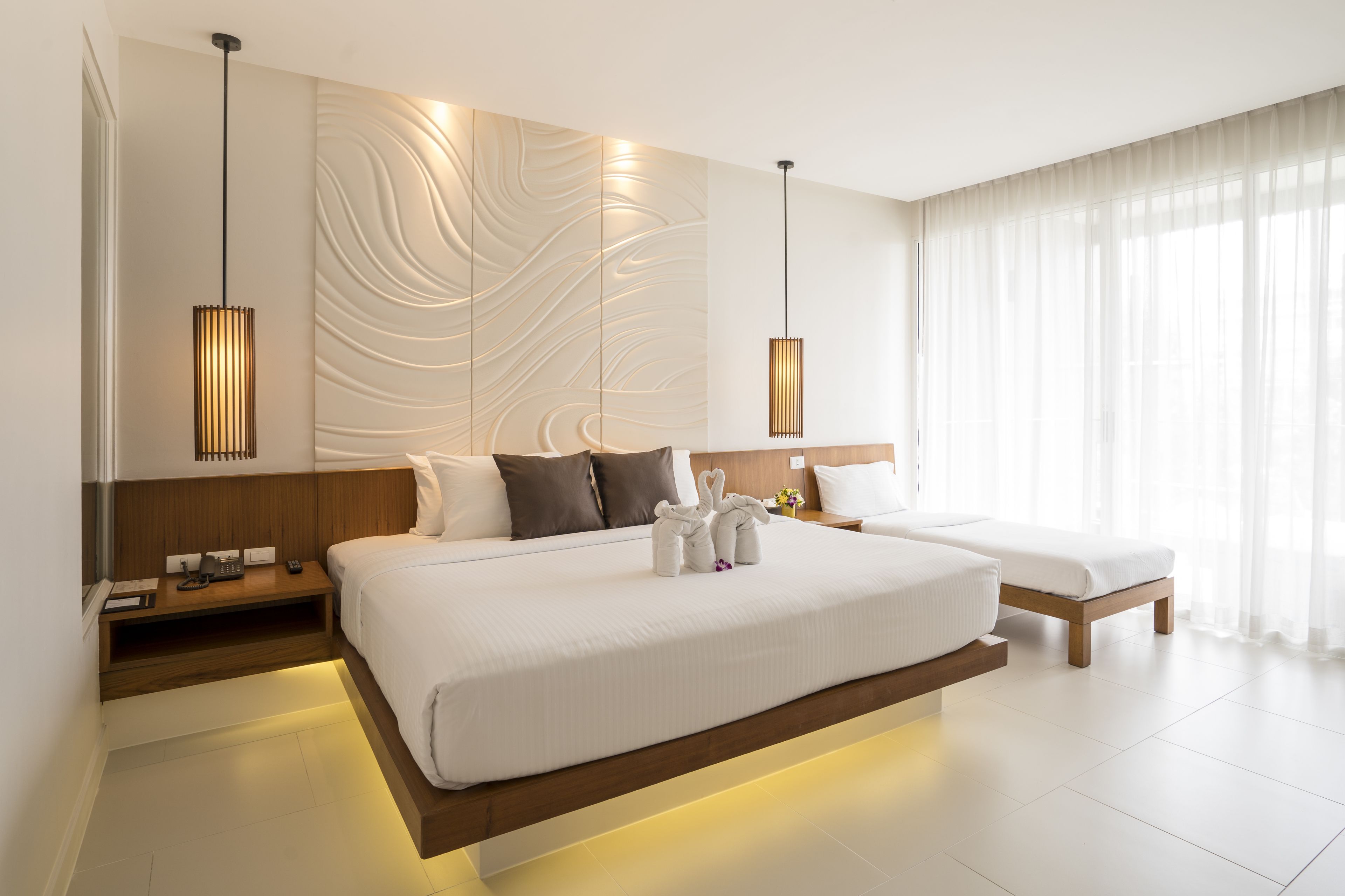 Quarto de hotel moderno com uma cama grande, mesas de cabeceira e um detalhe decorativo na parede.