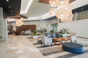 Um hall amplo com design moderno, com balcão de recepção, área de estar com sofás e poltronas, e iluminação decorativa.