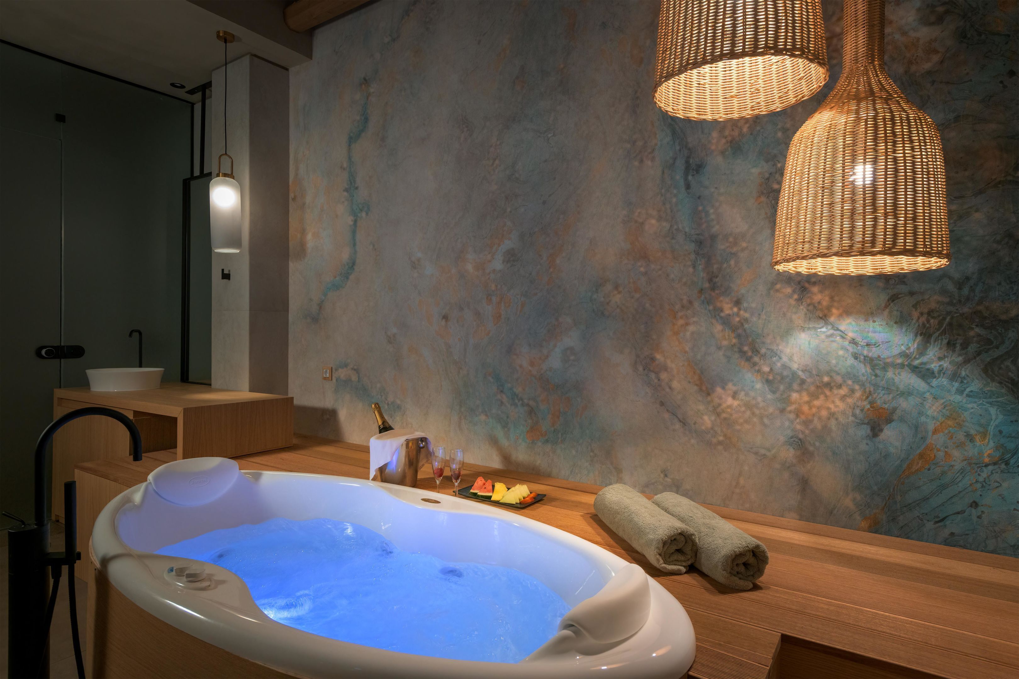 Uma área de spa com hidromassagem, balcão de madeira e duas luminárias pendentes de vime.