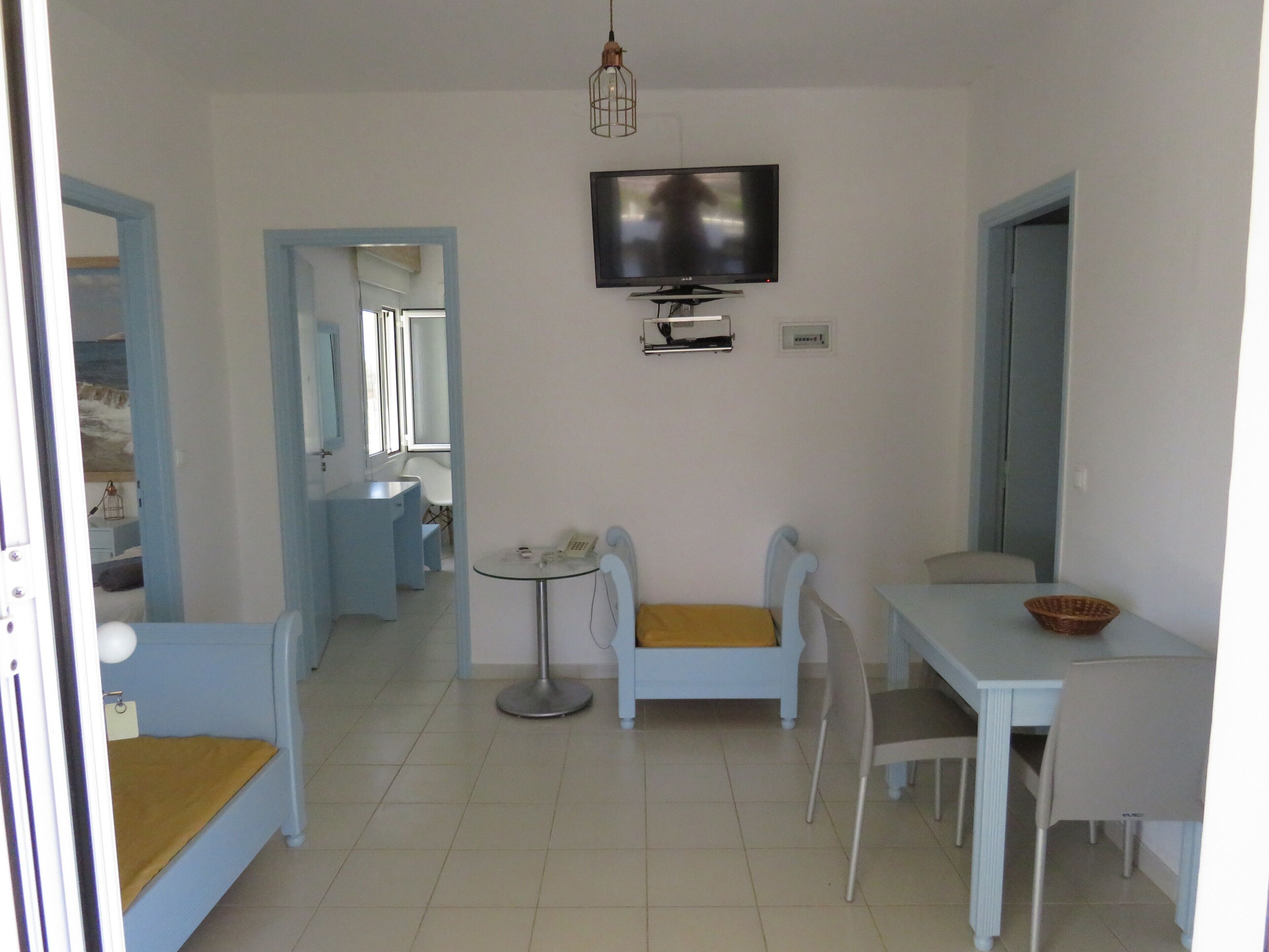 Quarto com uma mesa de jantar, cadeiras, uma TV fixada na parede e uma mesa redonda pequena com um telefone.