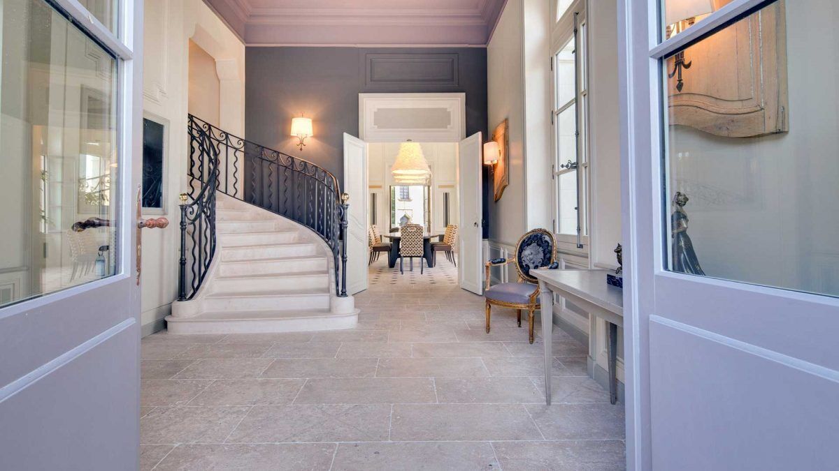Um corredor com escada, sala de jantar e uma estátua.