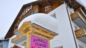 Placa de Albergo Sciatori Bar Ristorante, com telhado coberto de neve e varandas de madeira.
