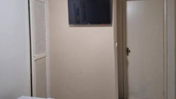 Quarto com chão em azulejos, porta, televisão na parede e pequeno frigorífico.