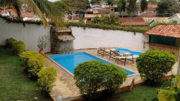 Um quintal com piscina, rodeado por um muro branco, pequenos arbustos e uma palmeira.