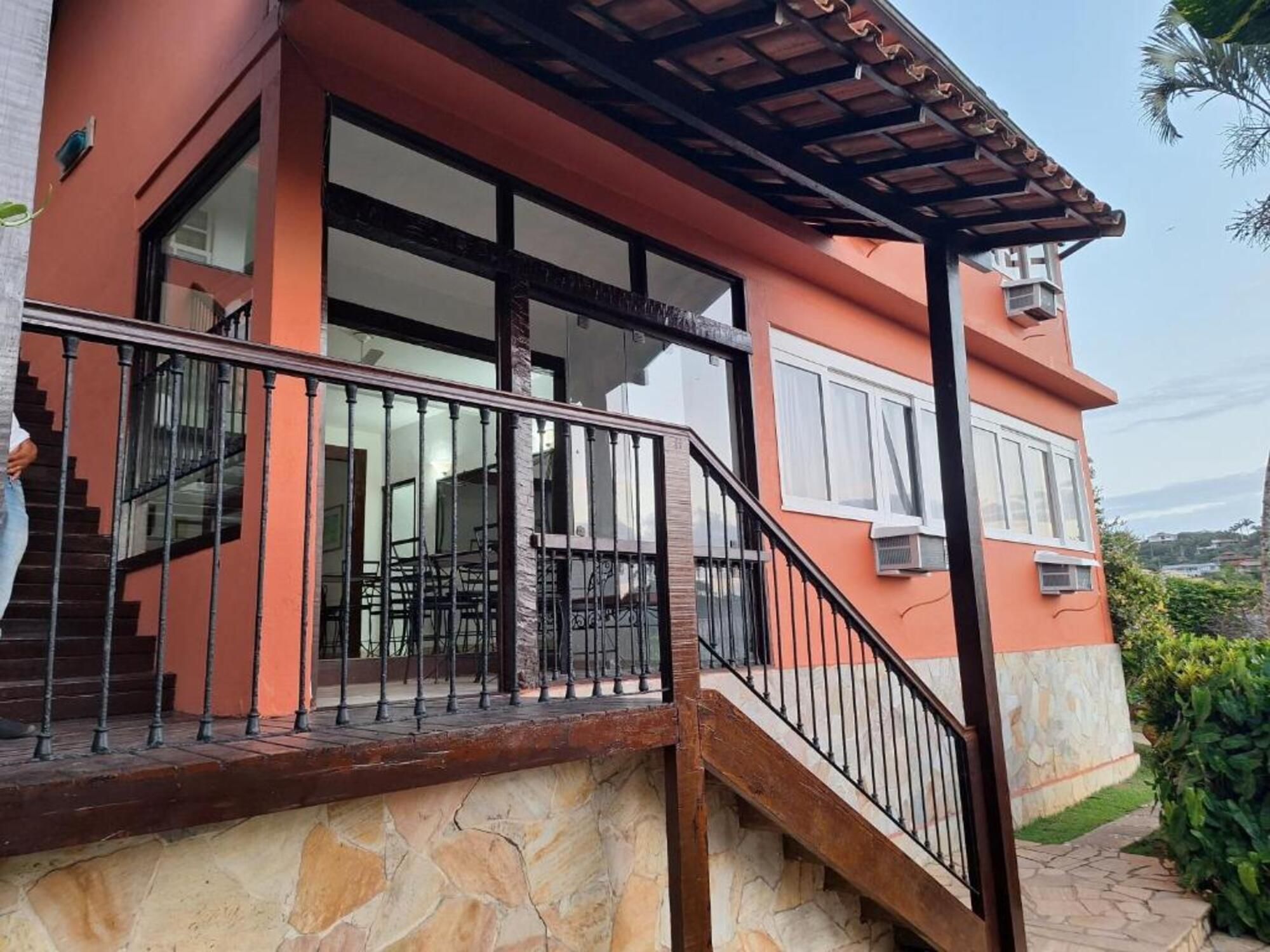 Um edifício com fundação de pedra, uma varanda com grades de metal e uma escadaria que leva à entrada.