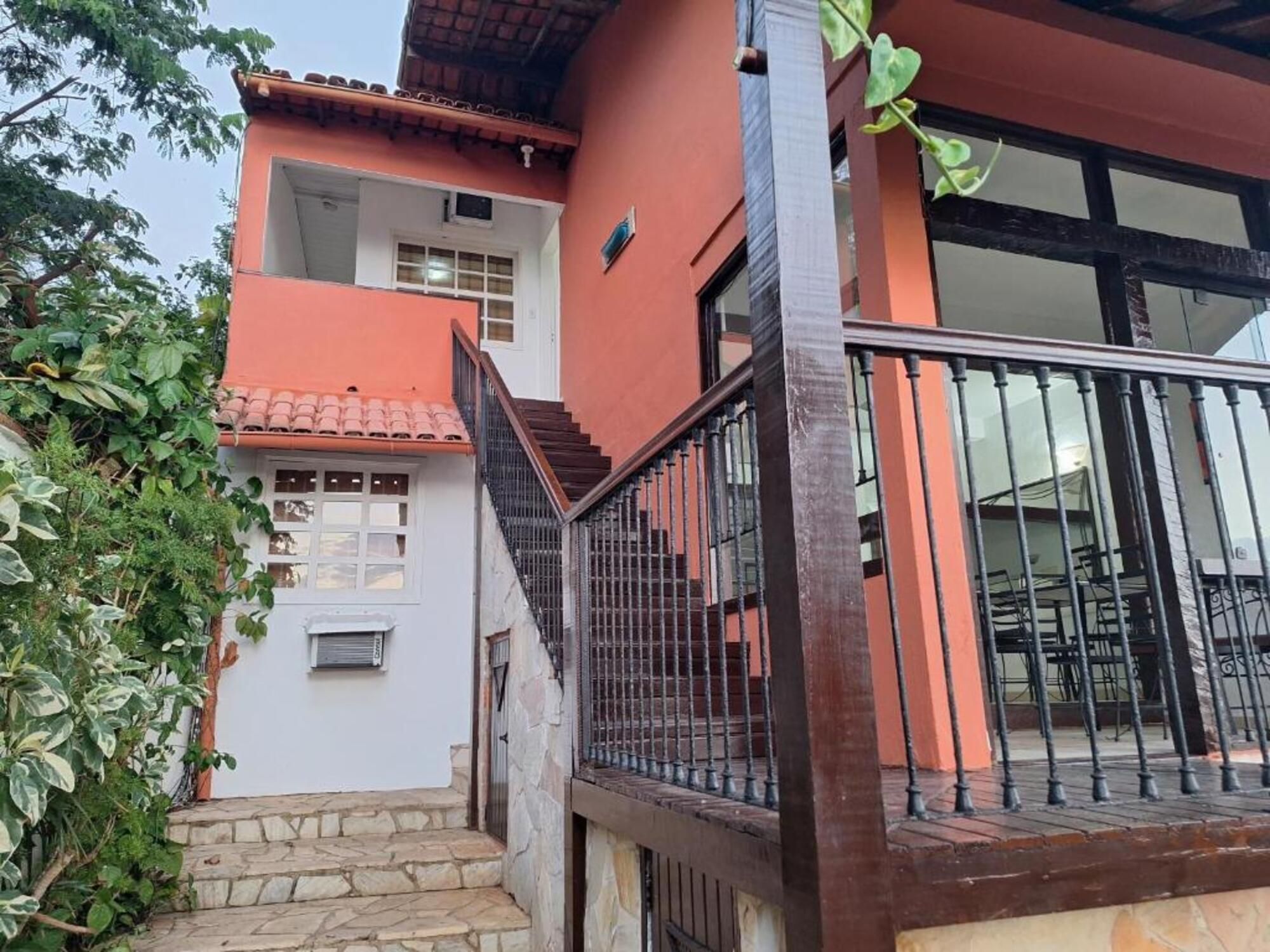 Edifício de dois andares com fachada vermelha, escadaria que leva ao andar superior e varanda com grade de metal.