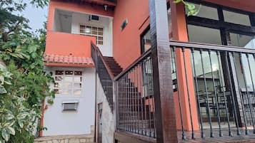 Edifício de dois andares com fachada vermelha, escadaria que leva ao andar superior e varanda com grade de metal.