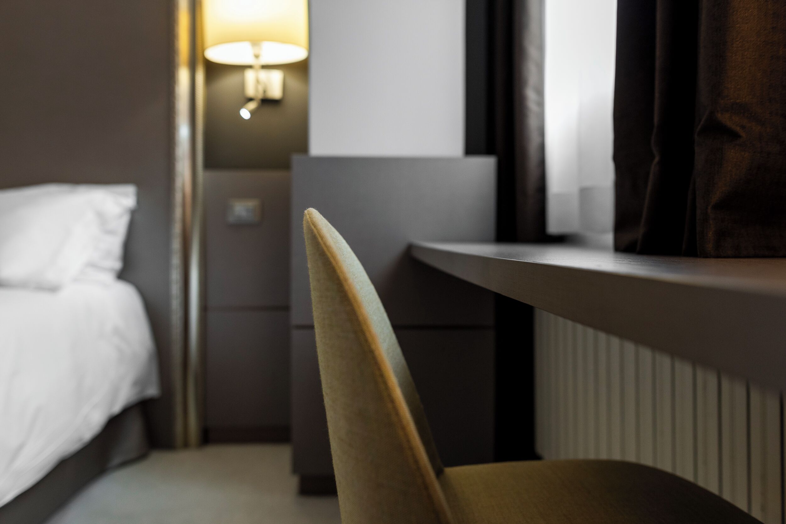 Quarto de hotel com uma cama, uma cadeira, uma mesa de cabeceira e um abajur.