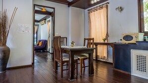 Uma área de refeições com cadeiras de madeira e uma mesa, um micro-ondas no balcão e uma janela com cortinas.
