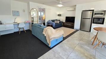 Uma sala de estar moderna com sofá, TV e área de cozinha, incluindo geladeira e micro-ondas.