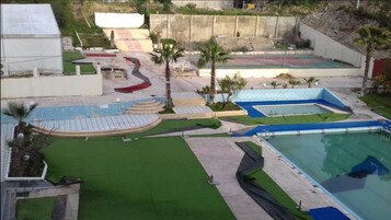 Área de piscina com um pequeno deck, palmeiras e um caminho vermelho.