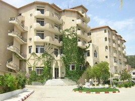 Um edifício residencial com vários andares, varandas, uma entrada central e um jardim ajardinado.