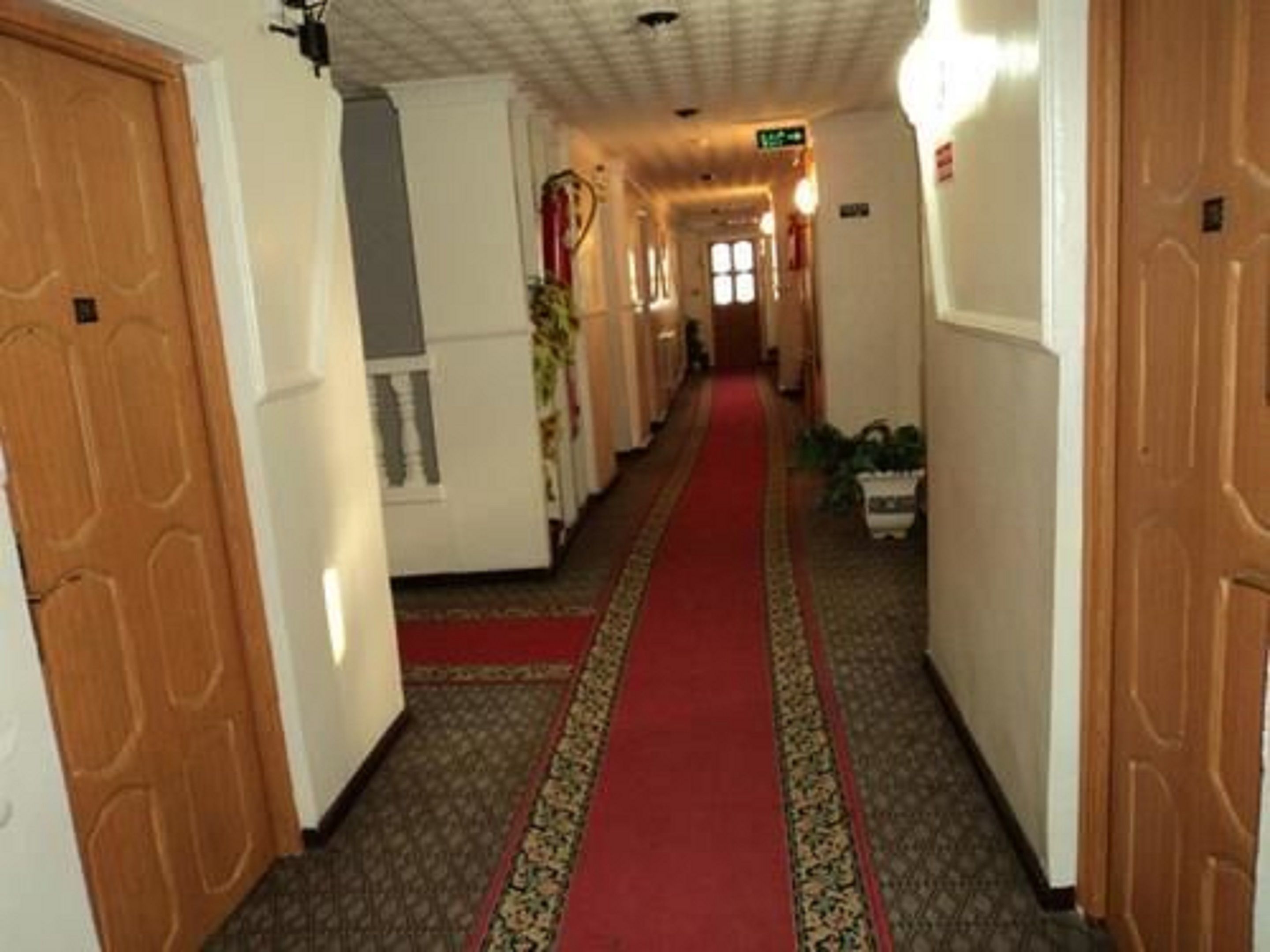 Um corredor de hotel com portas de madeira, tapete vermelho e piso estampado.
