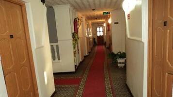 Um corredor de hotel com portas de madeira, tapete vermelho e piso estampado.